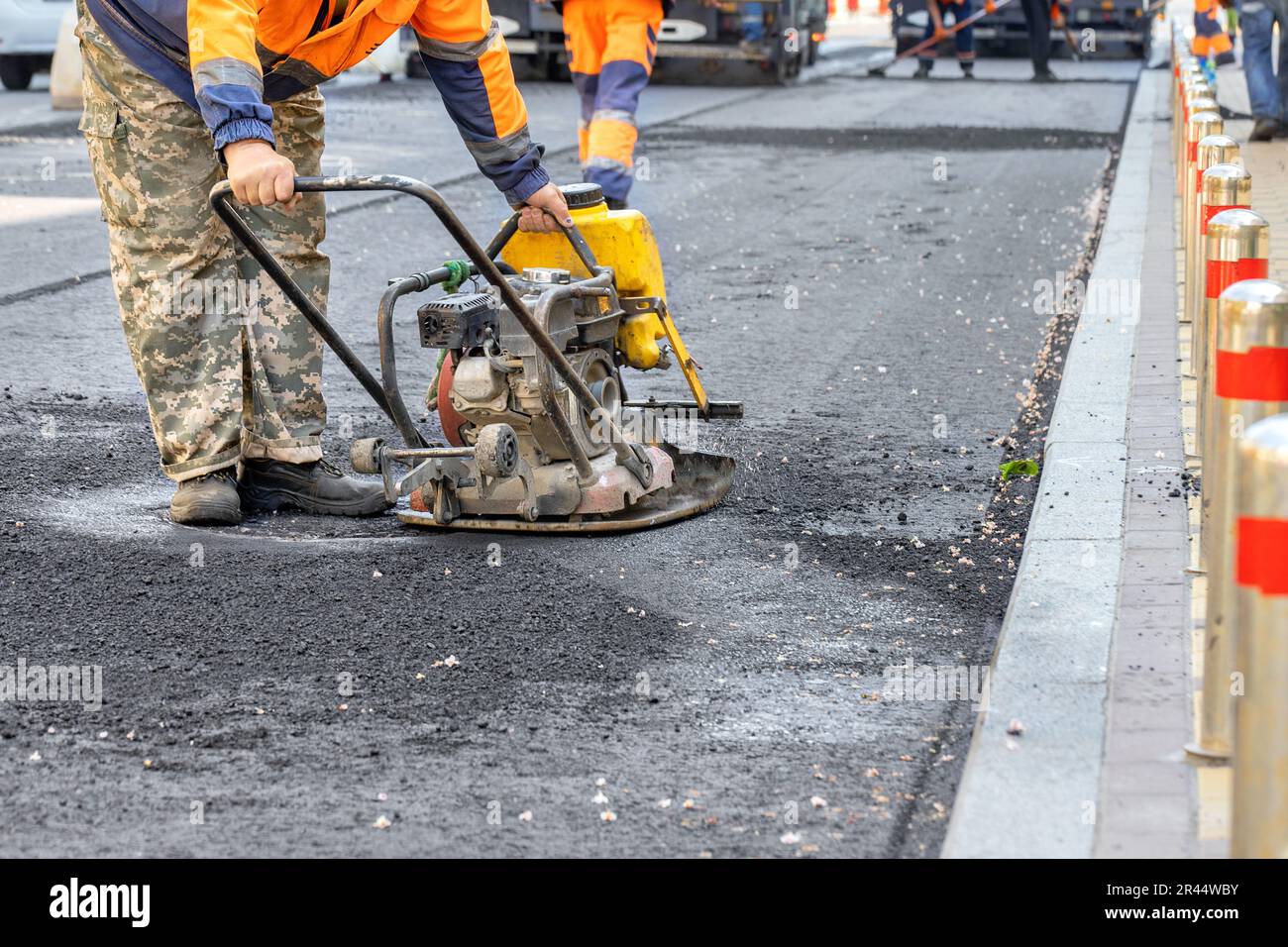 A road worker repairs a section of road by compacting fresh asphalt ...
