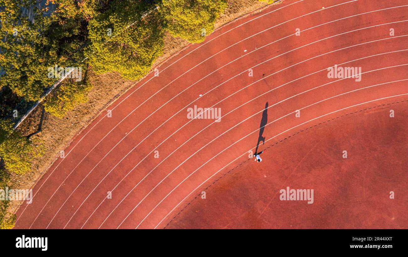 An aerial view of a person running on a running track with the sun ...