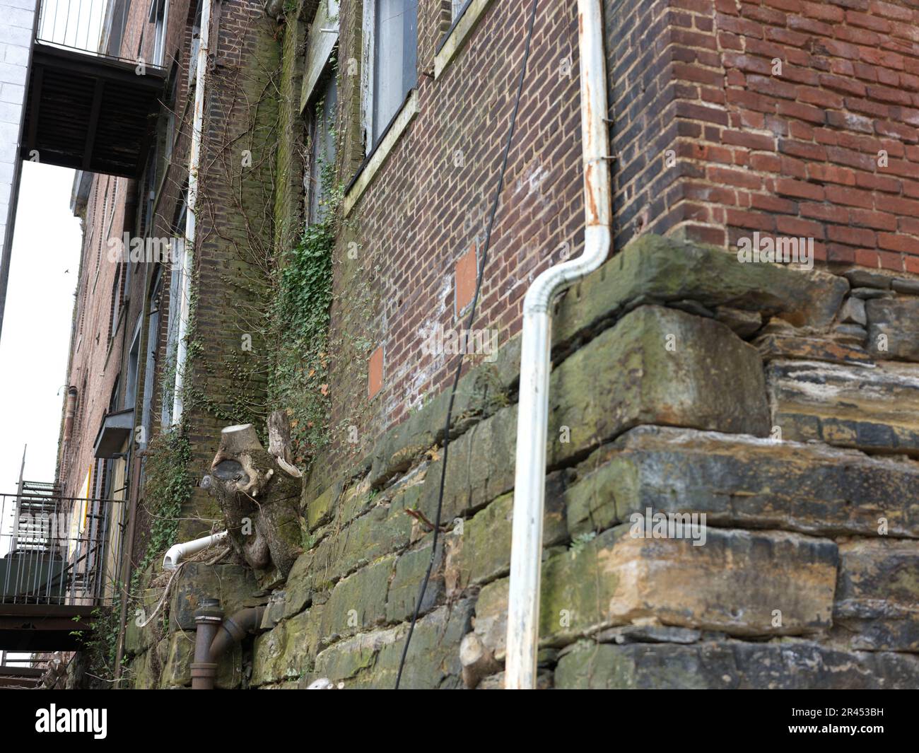 A white plumbing pipe running down the side of a red brick wall of a ...