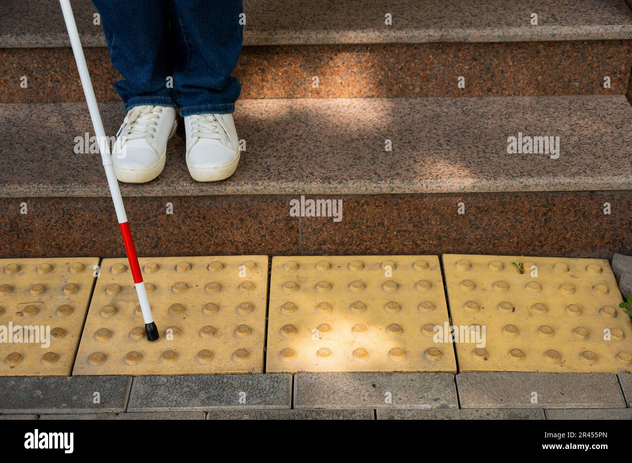 Close-up of female foot, walking stick and tactile tiles. Blind woman ...