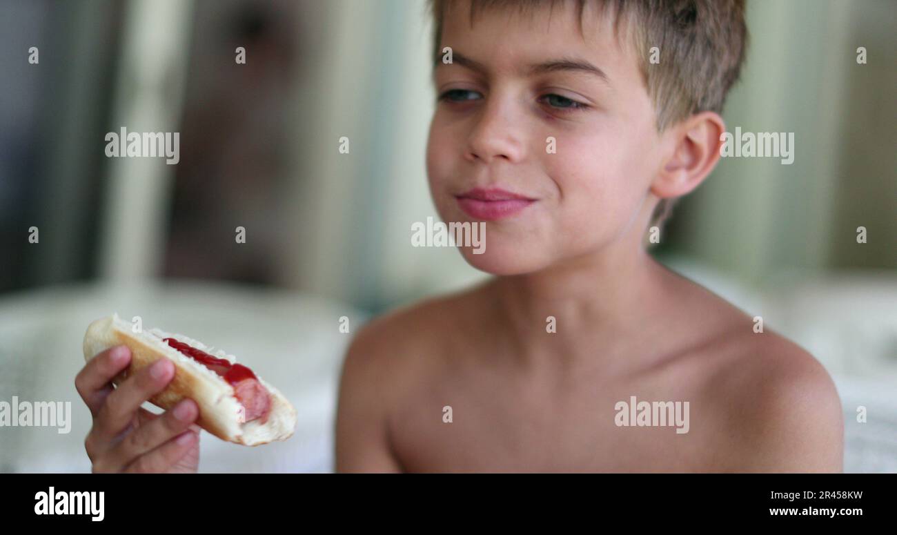 Child eating hot-dog outside. Young boy taking a bite of sausage with ...
