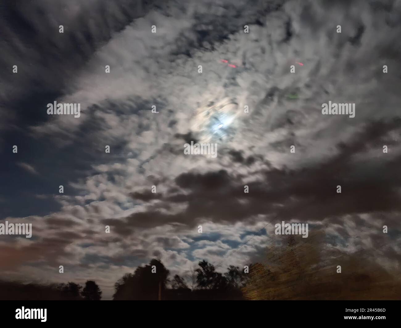 A dramatic night sky featuring dark clouds illuminated by the moonlight ...