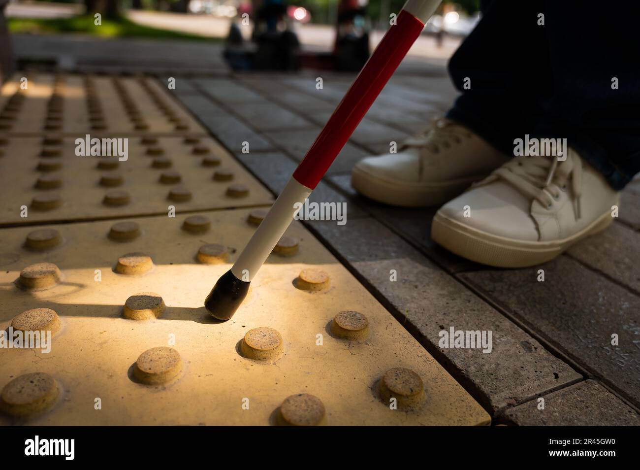 A close-up of a woman's feet with a tactile cane and a tactile tile ...