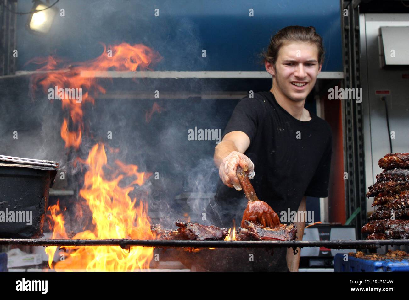 A male chef cooking barbecued food on an outdoor grill, with flames ...