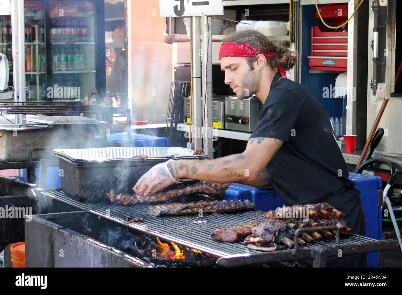 A male chef cooking barbecued food on an outdoor grill, with flames ...