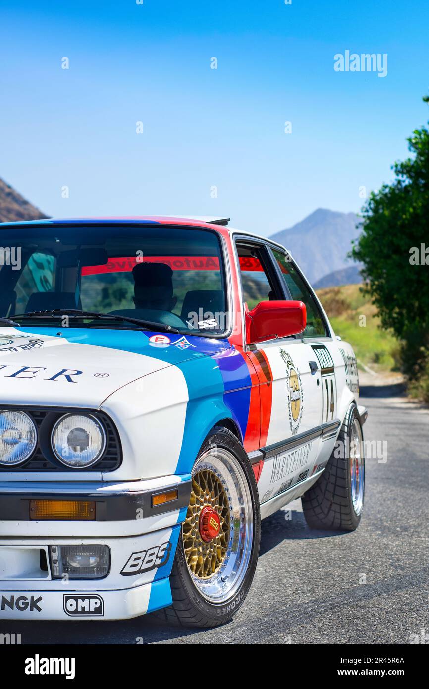 A blue and white E30 BMW parked in the middle of a two-lane asphalt ...