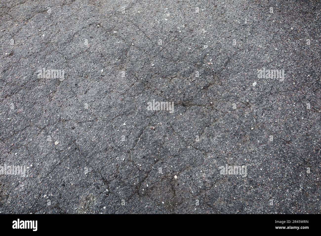 Broken grey asphalt road which is cracked. There are gravels on the ...