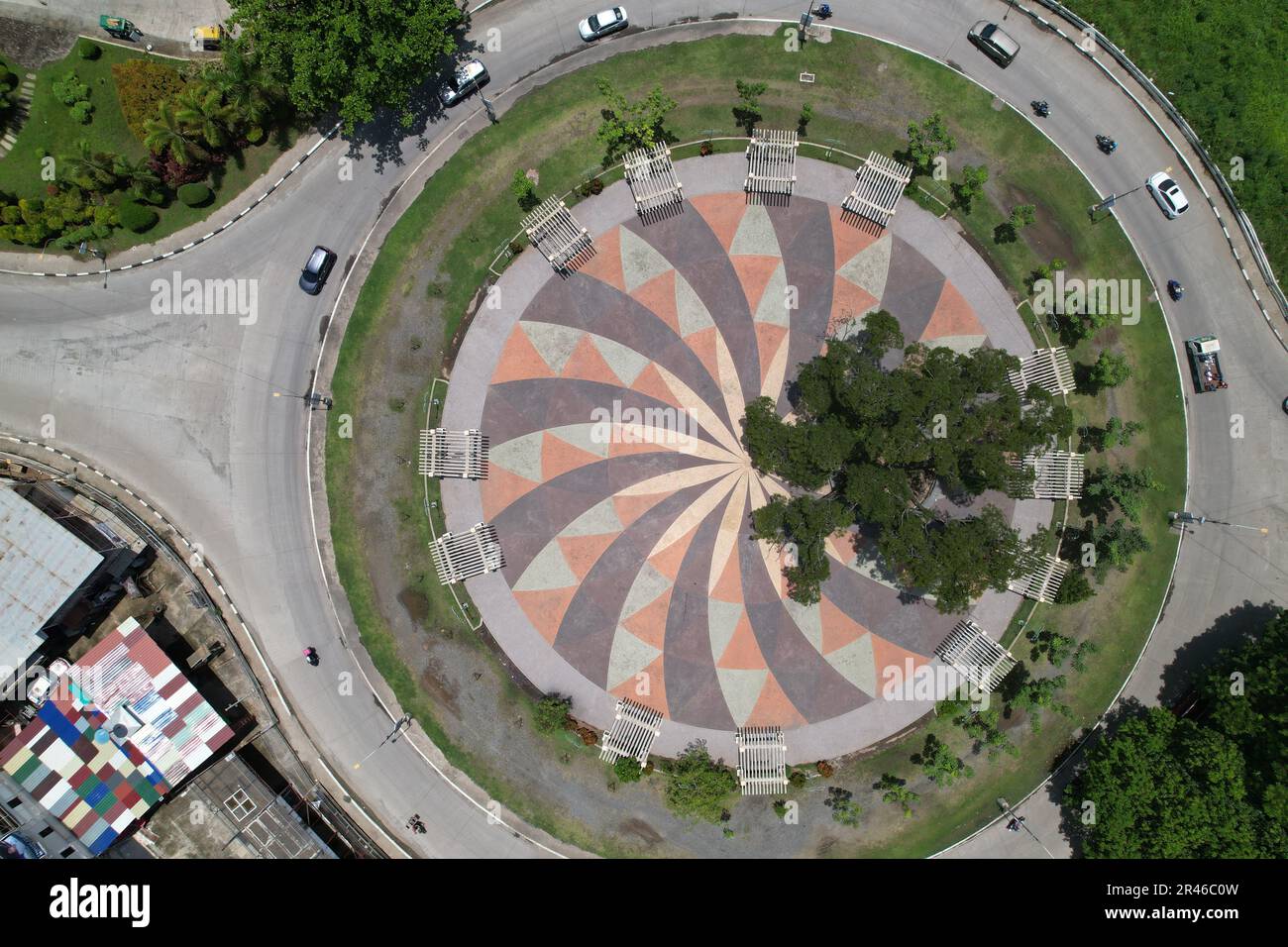An aerial view of a roundabout with green trees and passing cars ...