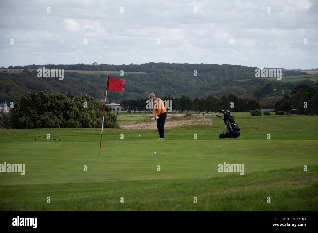 A Caucasian male wearing golf attire stands on a golf course, readying ...