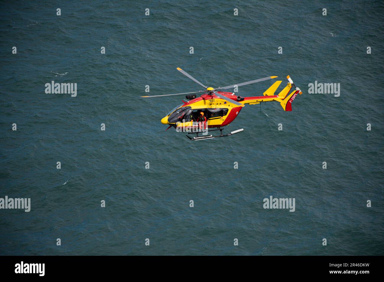 A bright yellow helicopter with a person in the cockpit hovering over a ...