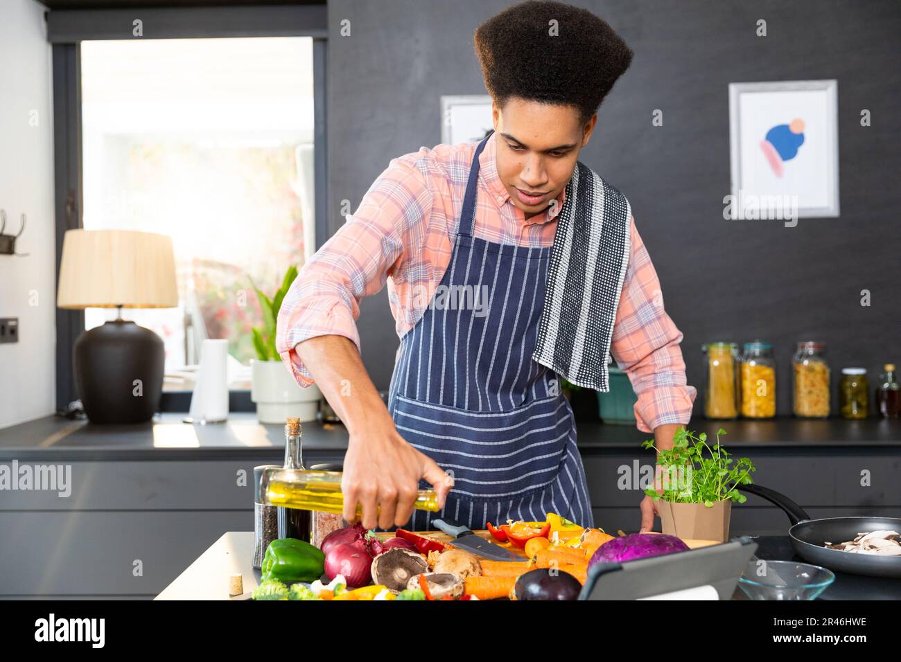 Biracial man wearing apron cooking dinner, pouring vegetables with oil ...
