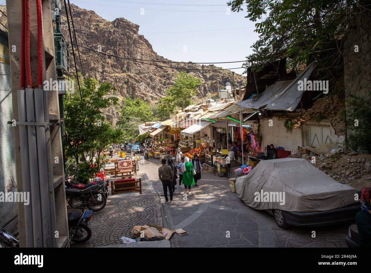 The people walking down the narrow urban street with shops in Iran ...