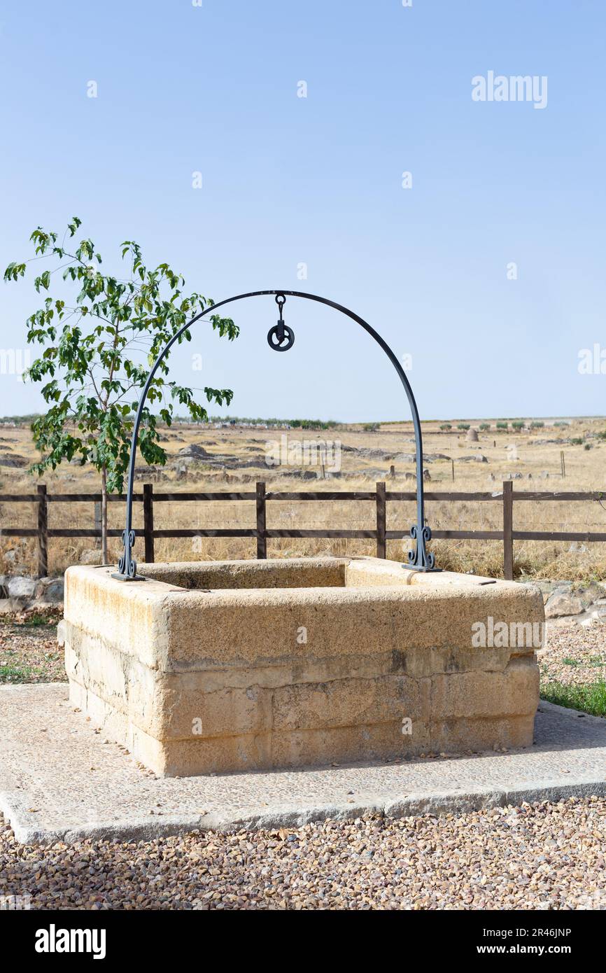 Stone well for water in middle of field. Has metal arch. It is on ...