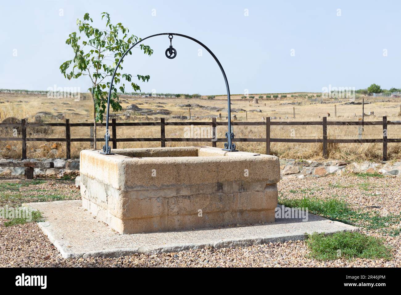 Stone well for water in middle of field. Has metal arch. It is on ...