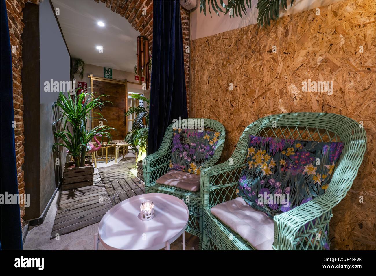Corridor of a beach-style nightclub with green wicker seats and sand on ...
