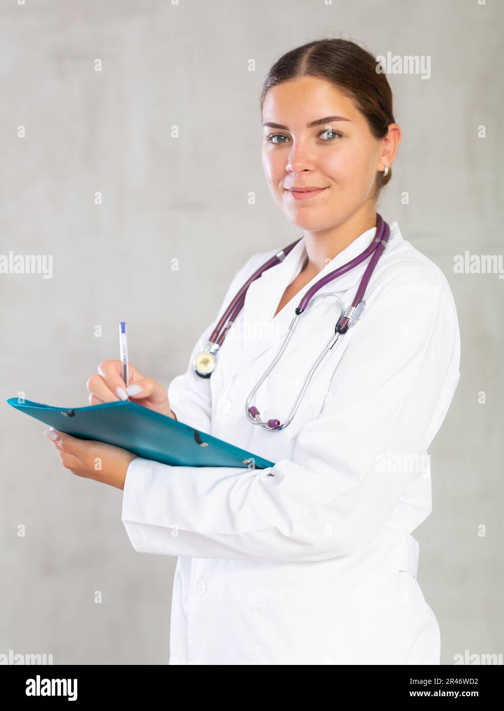 Happy female doctor standing and making notes in file Stock Photo - Alamy