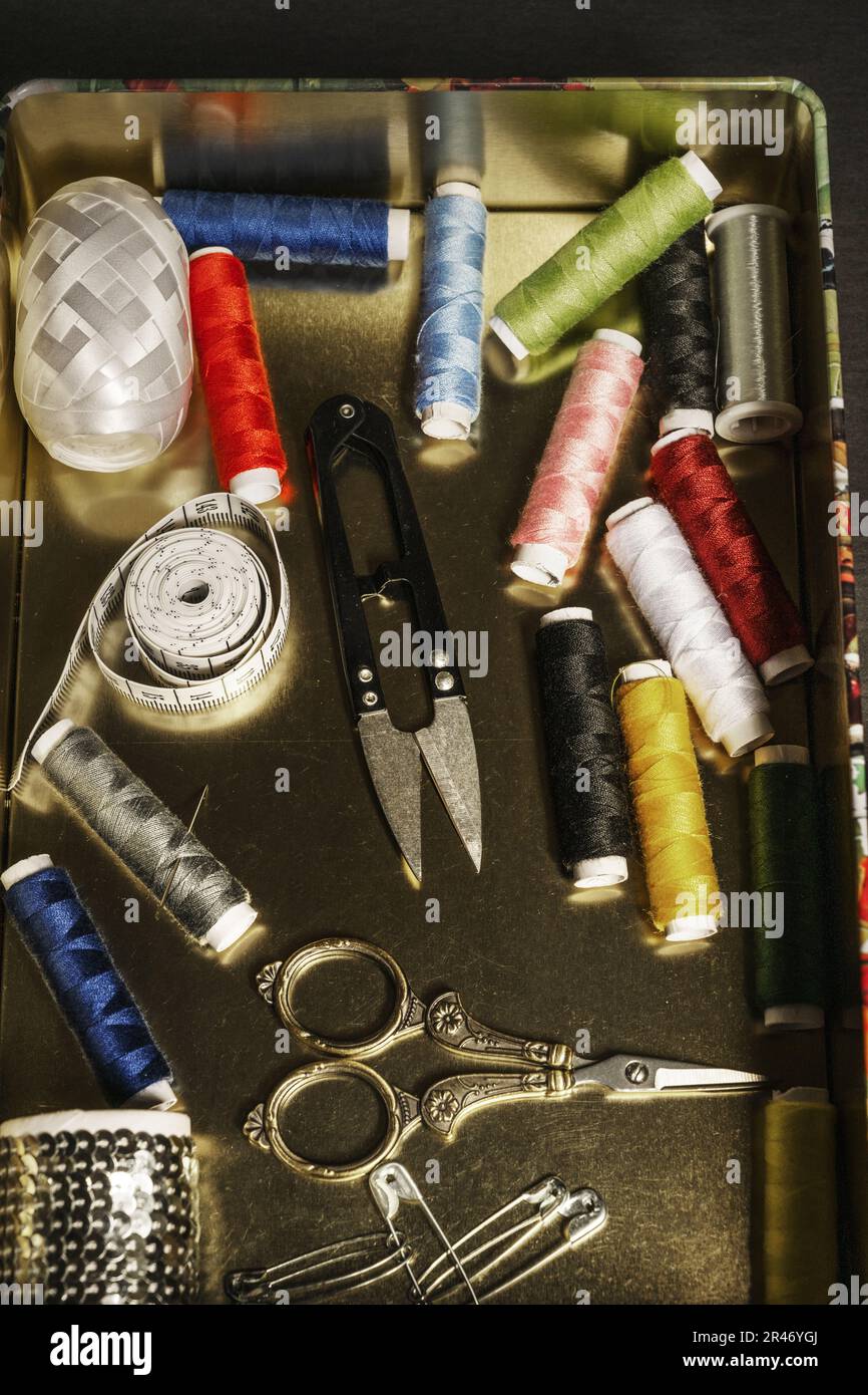 A metal box with sewing utensils, spools of thread, needles, scissors ...