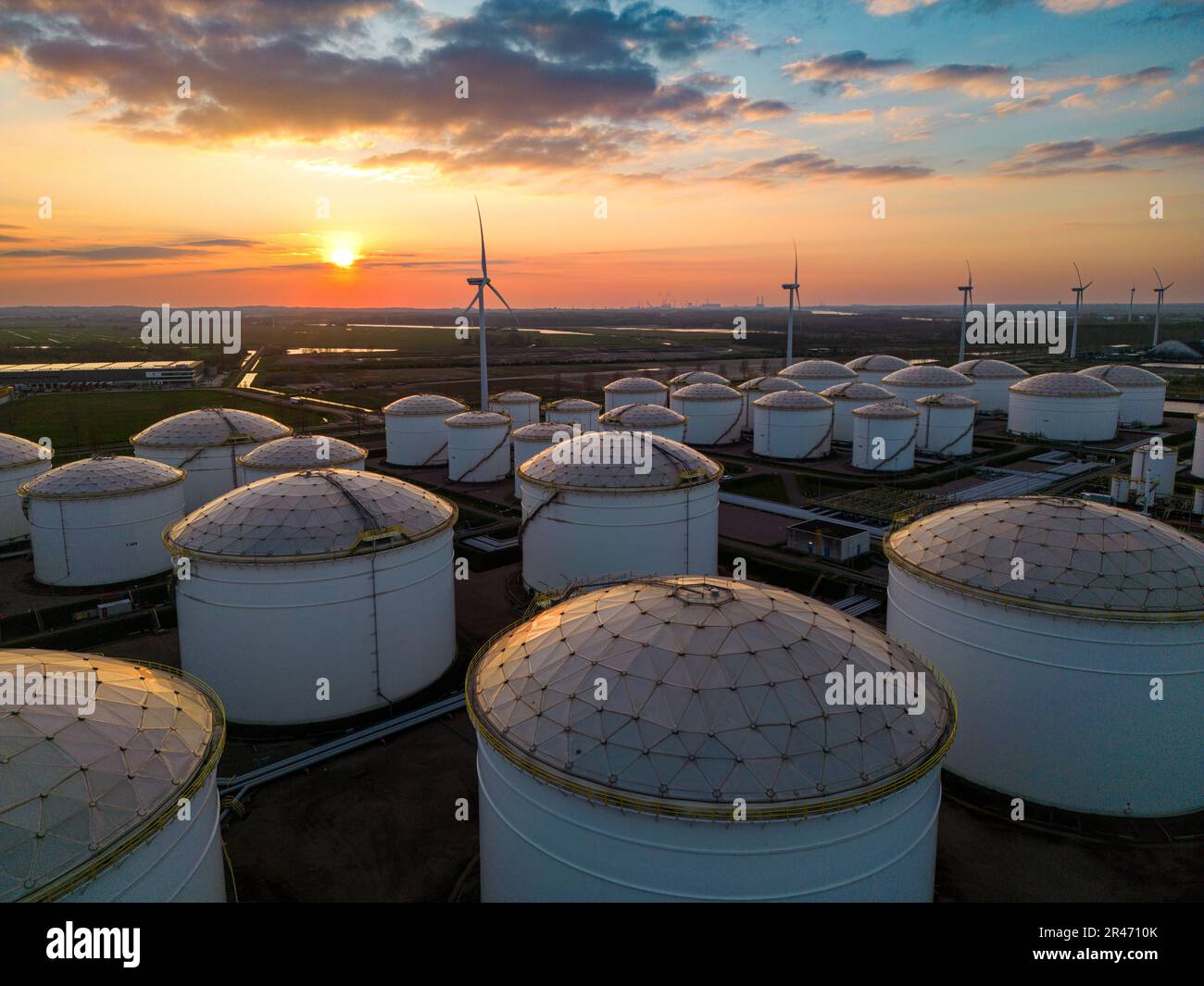 An aerial shot of the sunset behind an oil field filled with tanks and ...