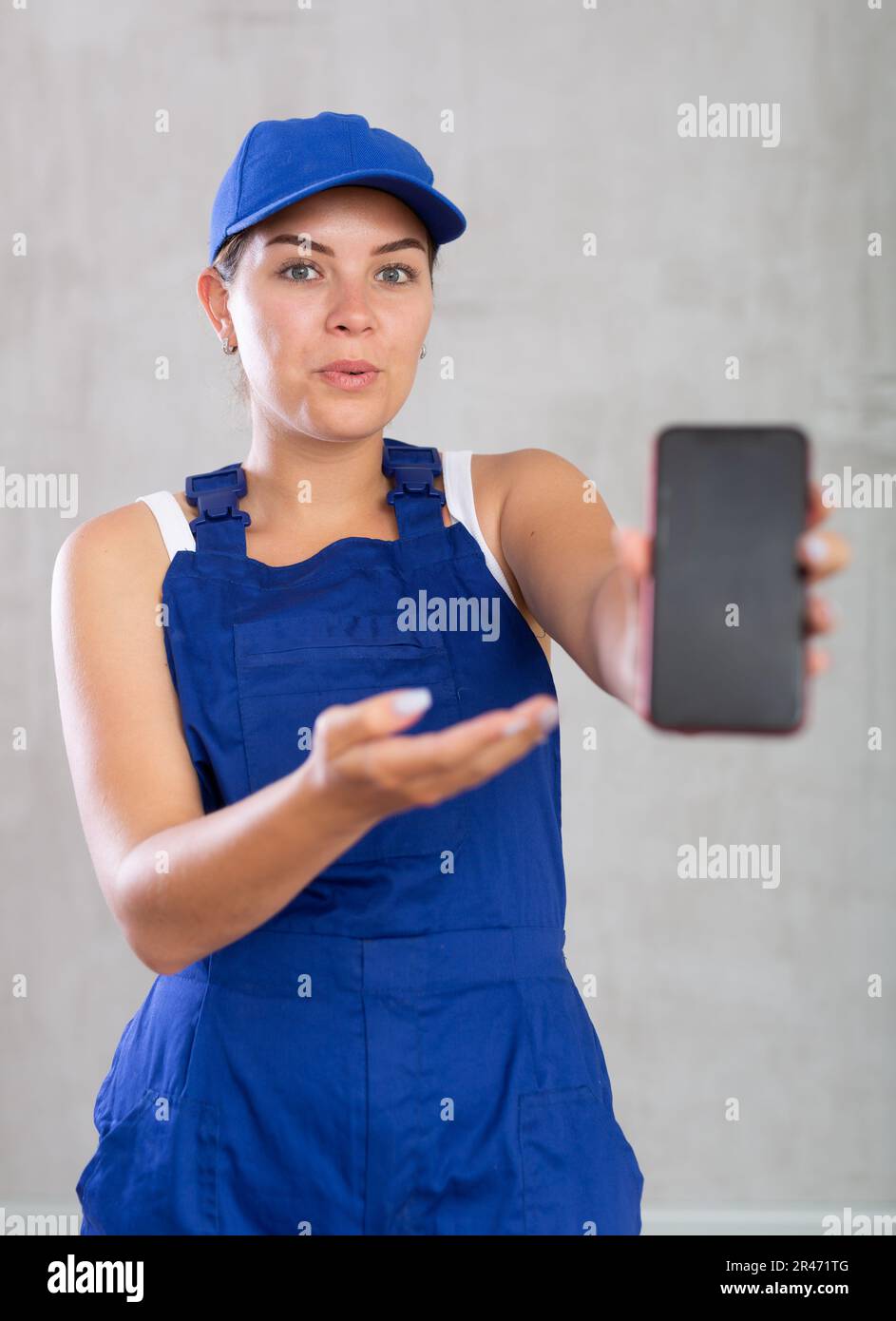 Happy female worker in work clothes showing screen of her smartphone ...