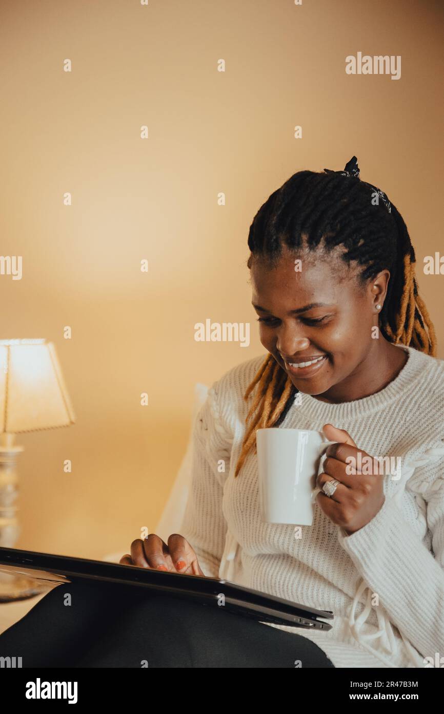 A young African woman using the gadget and enjoying a cup of coffee ...