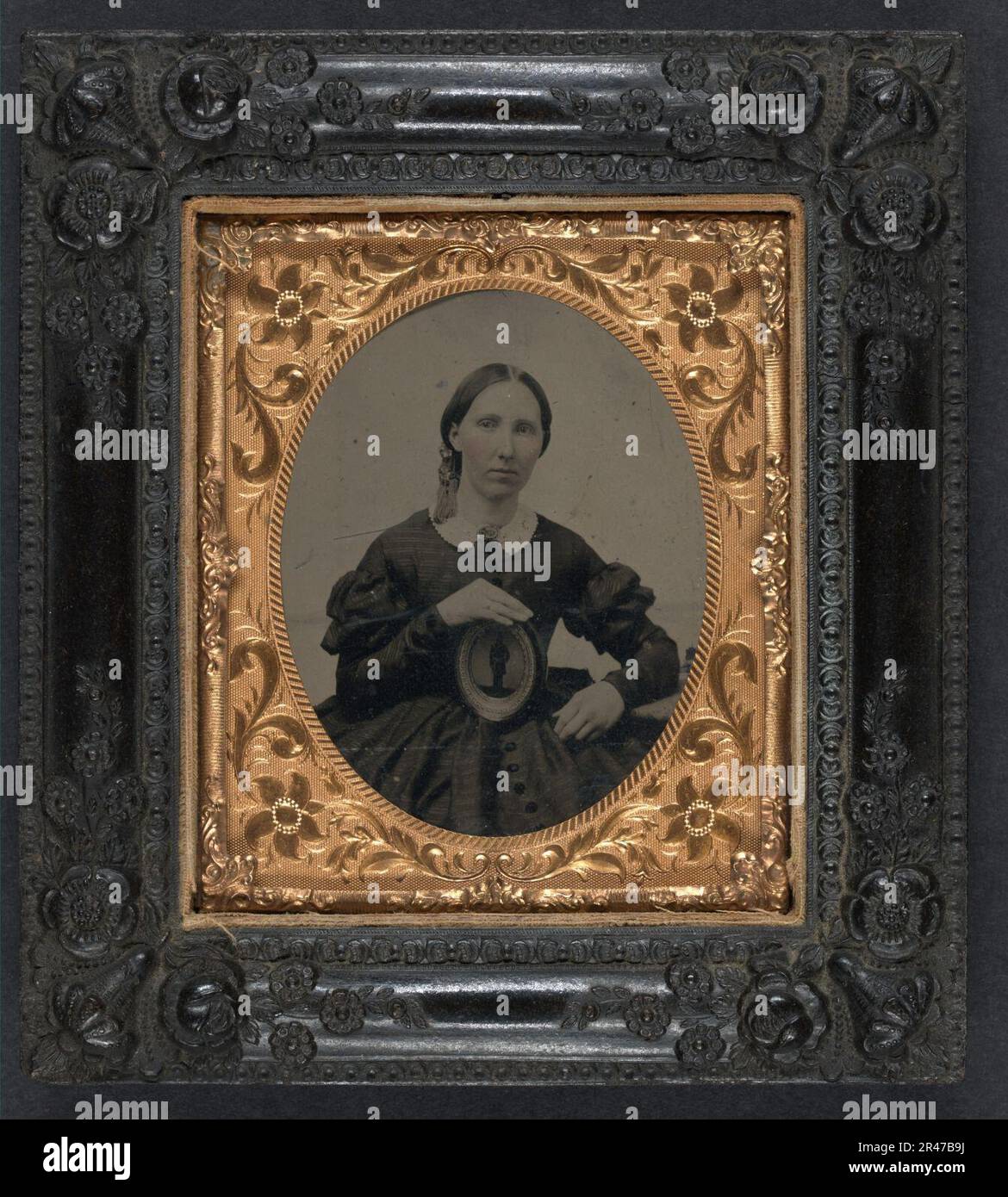 Unidentified woman wearing mourning brooch and displaying framed image ...