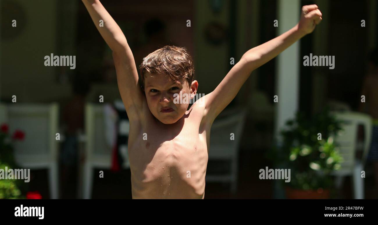 Child raising arms in the air in celebration. Excited young boy raises ...