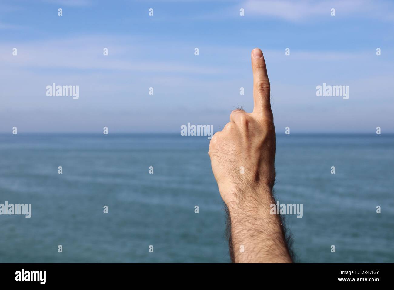 Hand doing,showing number gesture symbol one on blue summer sky nature ...