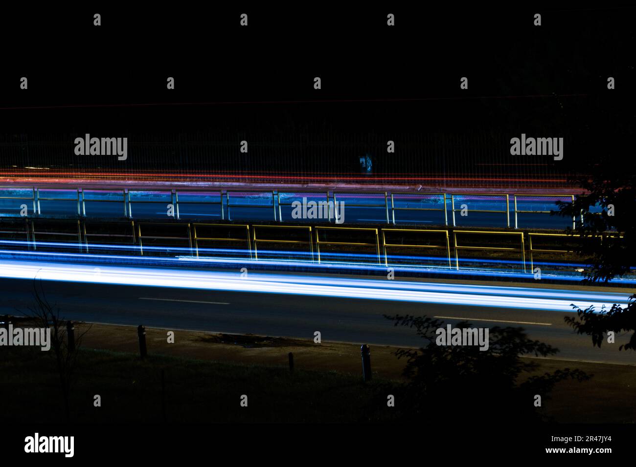 Colorful light trails streak across a road, illuminated by cars driving ...