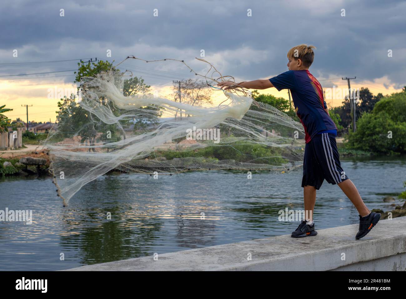 A young boy stands at the edge of a body of water, holding out a ...