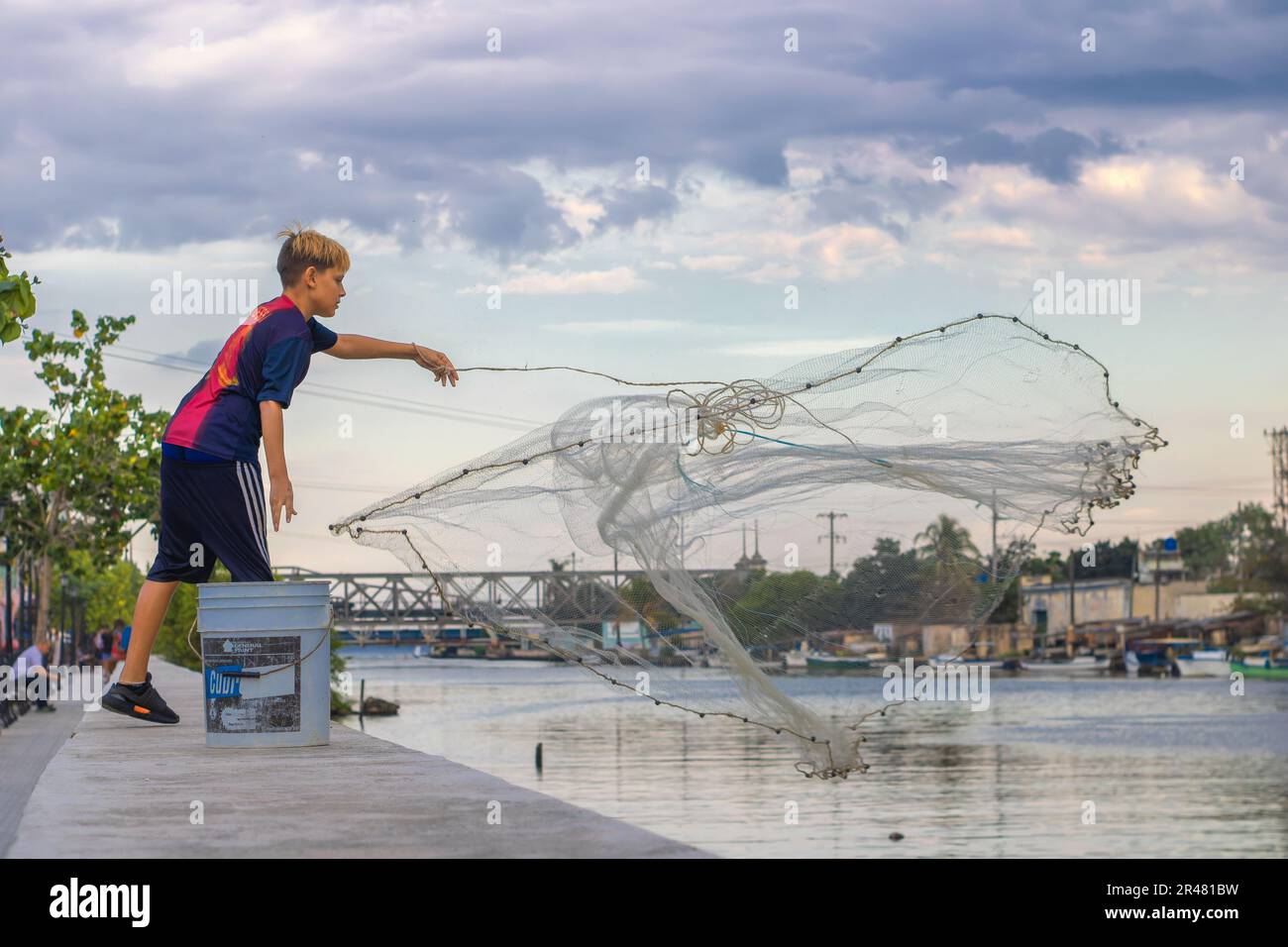 An adorable young boy throwing a fishing net into the water in an ...