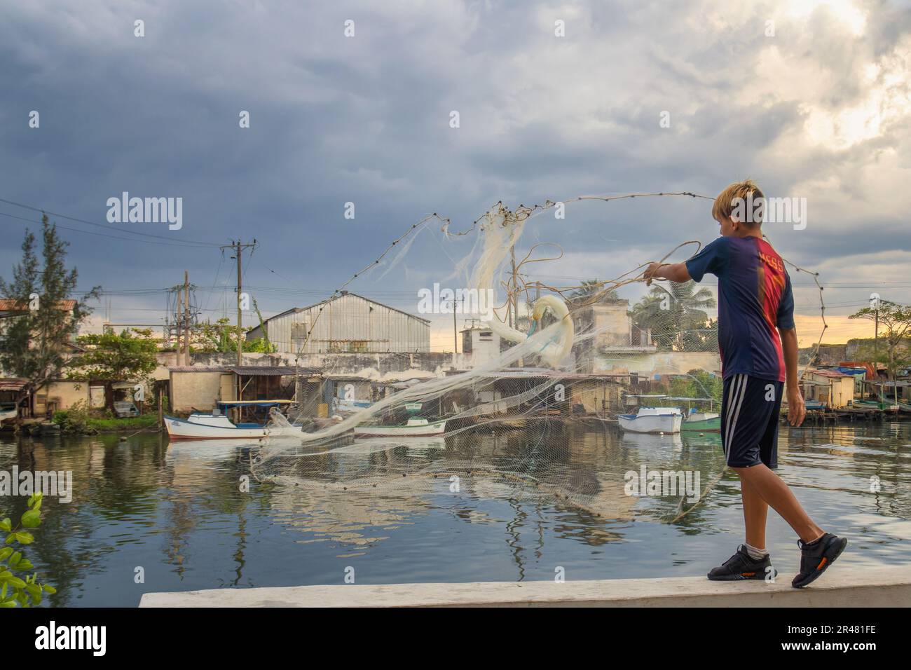 A young boy stands at the edge of a body of water, holding out a ...