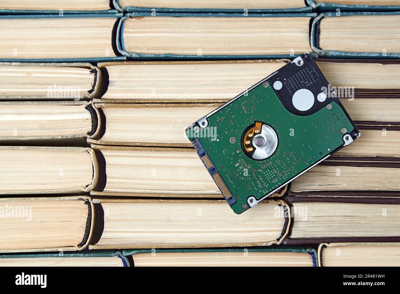 The hard drive of the computer lies on a pile of shabby paper books ...