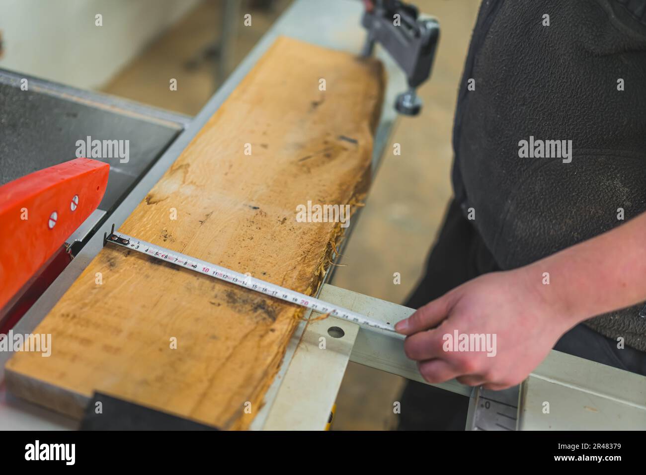Carpenter measuring wooden plank places on table before sawing it with ...