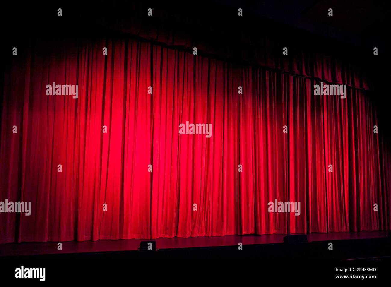 An illuminated theatrical stage with a voluminous draped red curtain ...