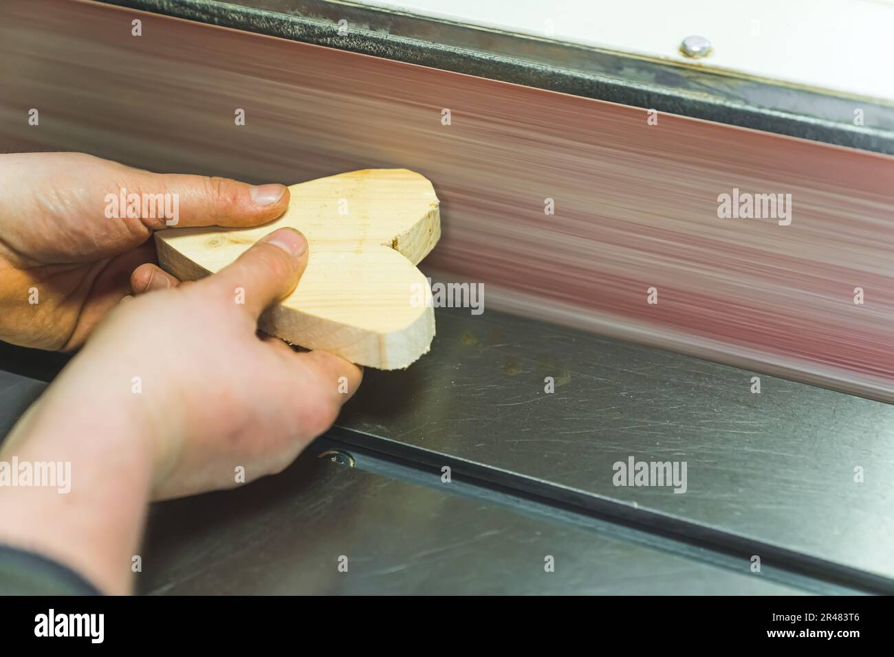 Hands of carpenter shaping edges of wooden heart using grinding machine ...