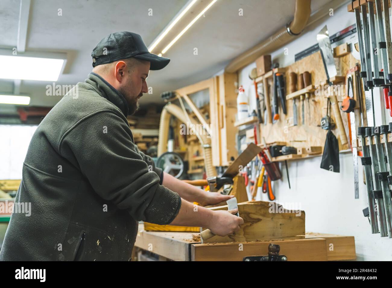 carpenter working on wood with a drawshave traditional tool in his workshop, medium shot. High ...