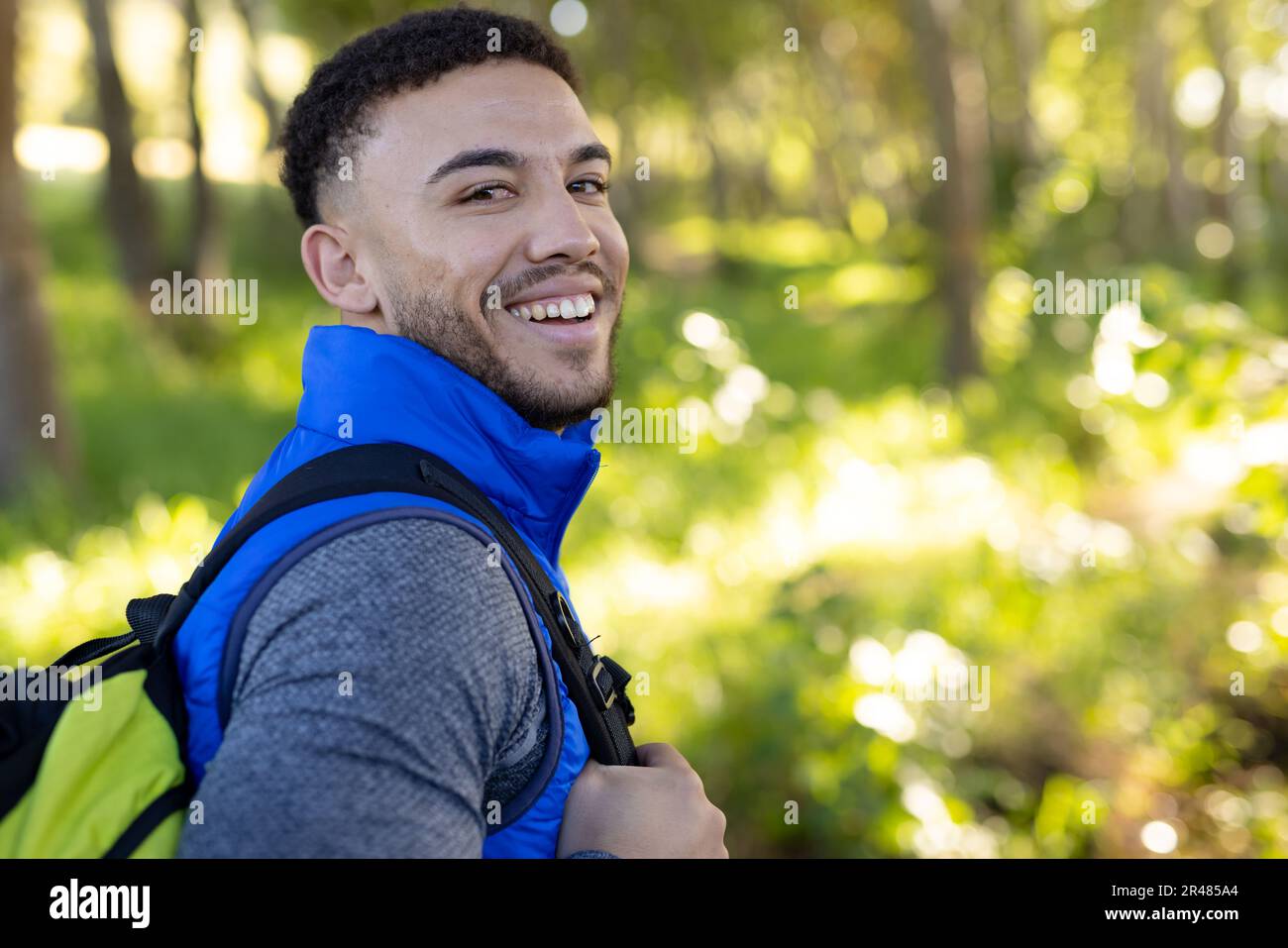 Portrait of happy biracial man looking at camera and smiling in forest ...