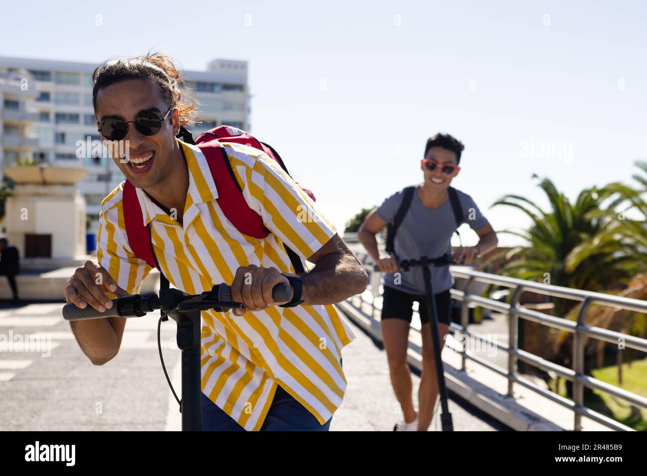 Happy Biracial Gay Male Couple Riding Scooters On Promenade By The Sea 8459