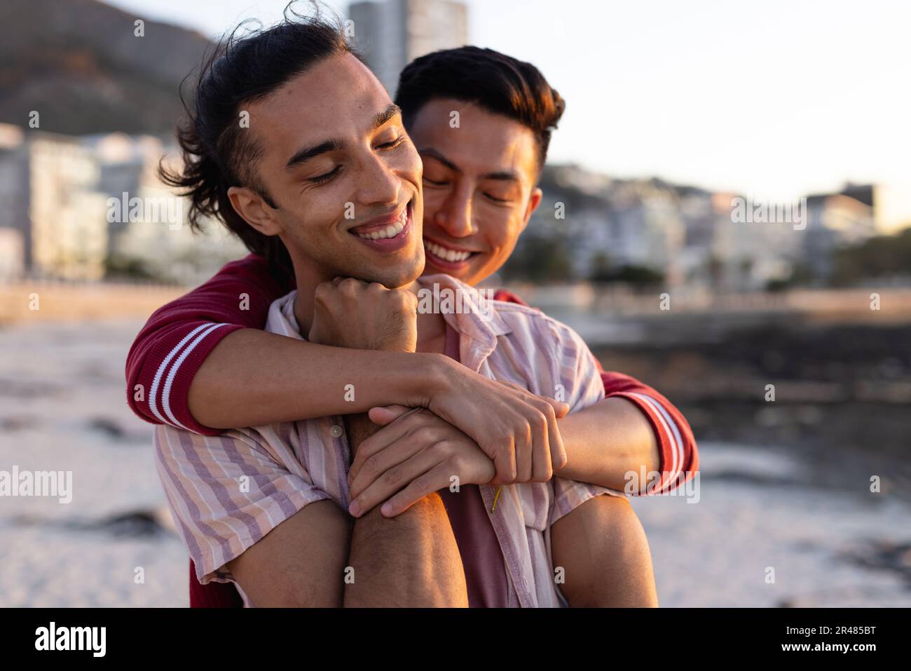 Happy biracial gay male couple embracing and smiling on beach at ...