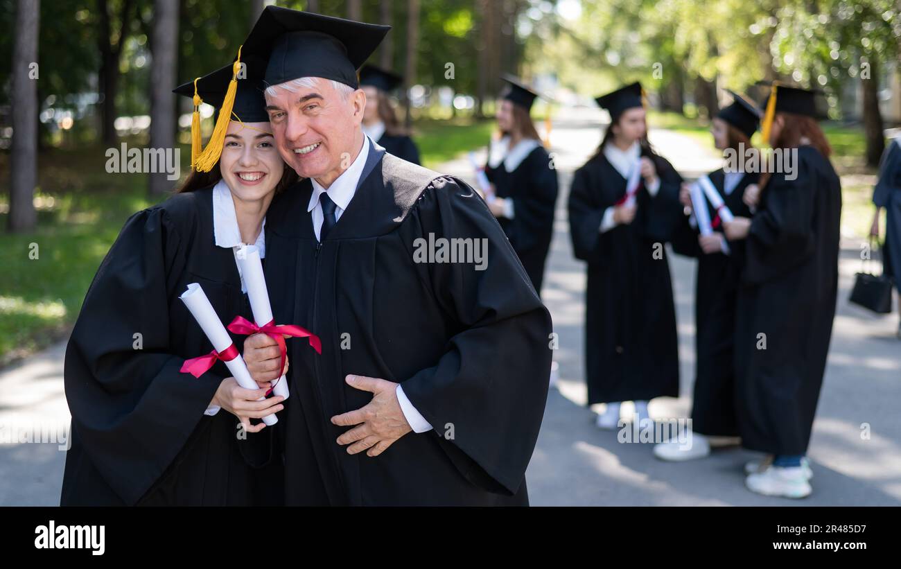 A group of graduates in robes outdoors. An elderly man and a young ...