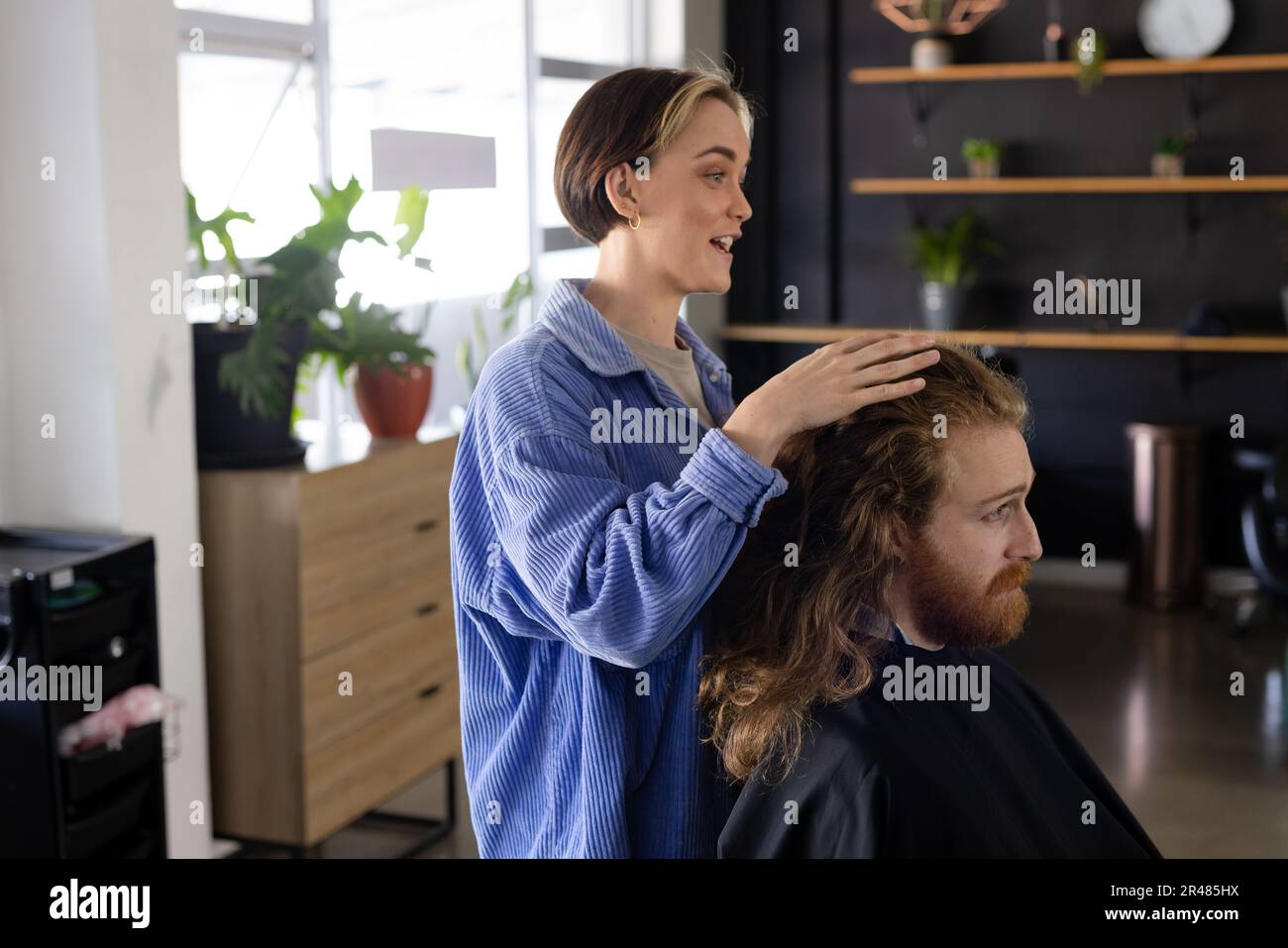 Happy caucasian female hairdresser talking and touching long hair of ...