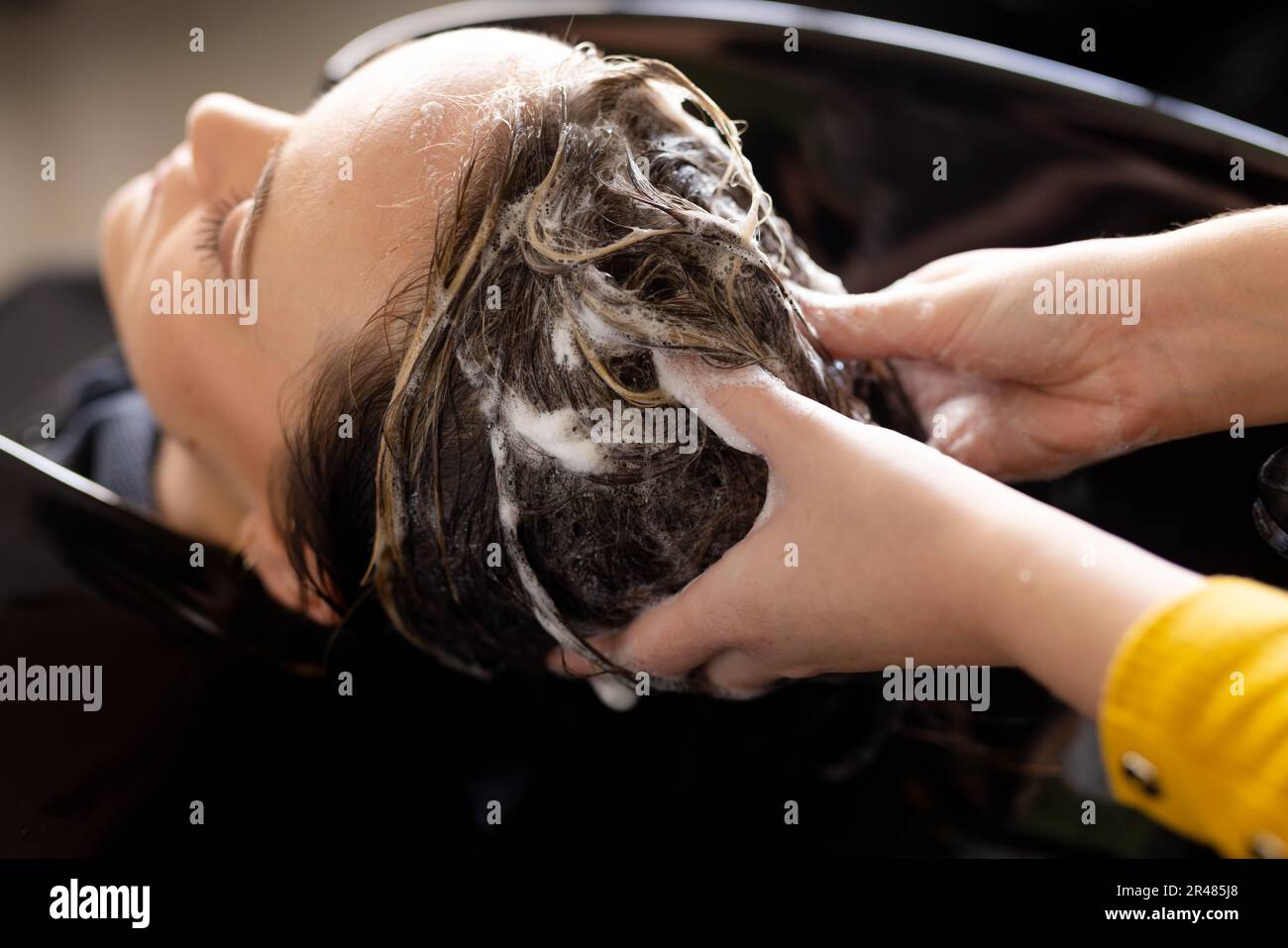 Hands of caucasian female hairdresser washing hair of relaxed female ...