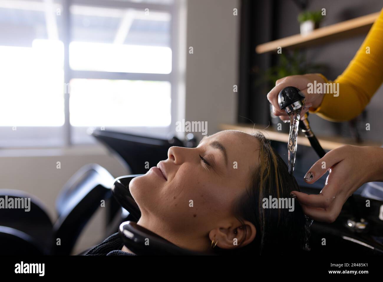 Hands of caucasian female hairdresser washing hair of relaxed, smiling ...