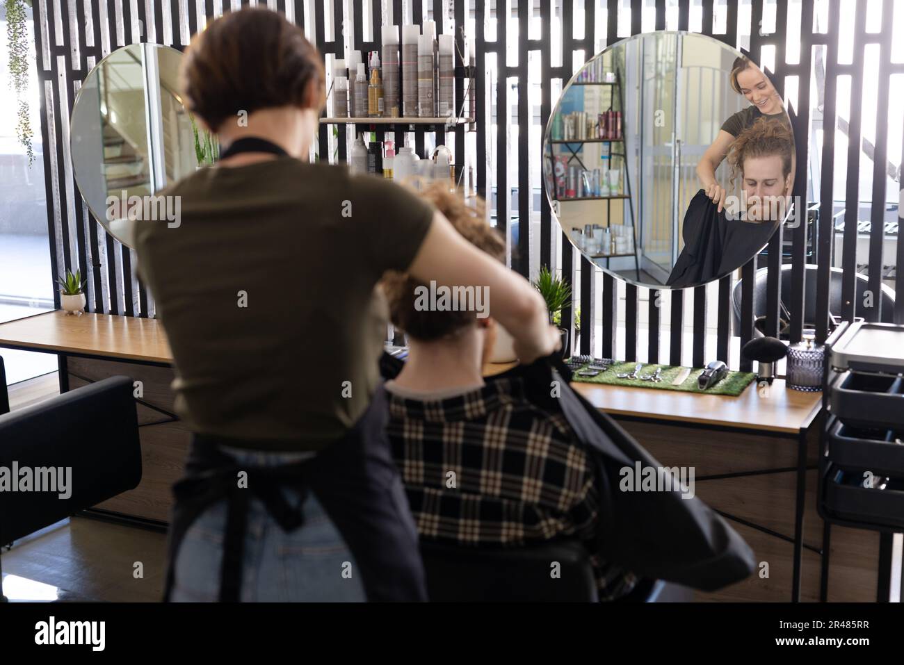 Caucasian female hairdresser putting cape on male customer before ...