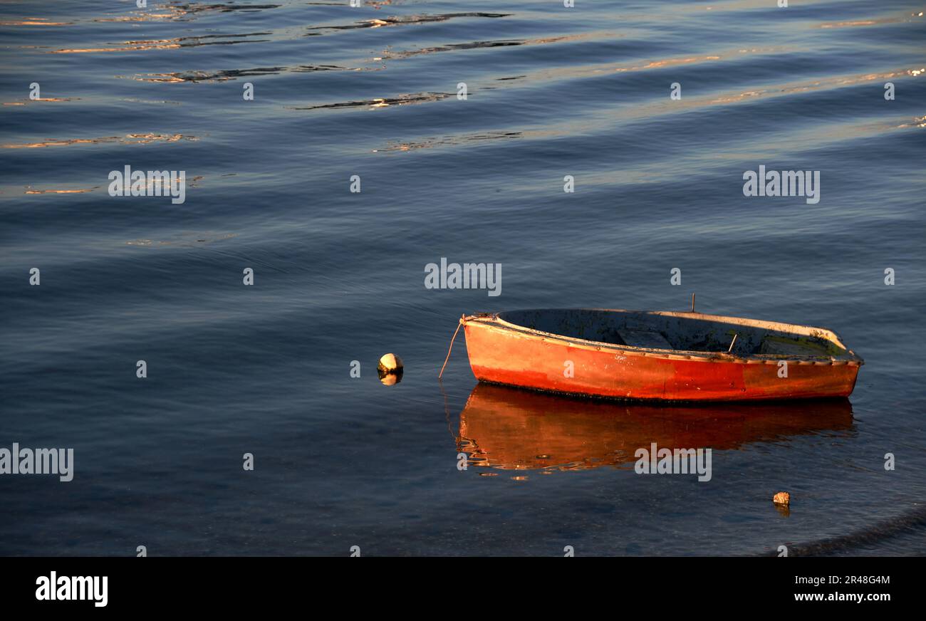 Small wooden fishing boat painted in orange color and anchored in the ...