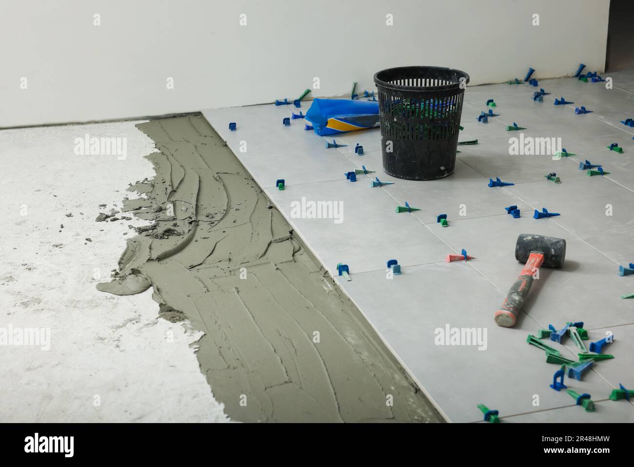 Beautiful tiles with wedges, tools and adhesive mix on floor near wall ...