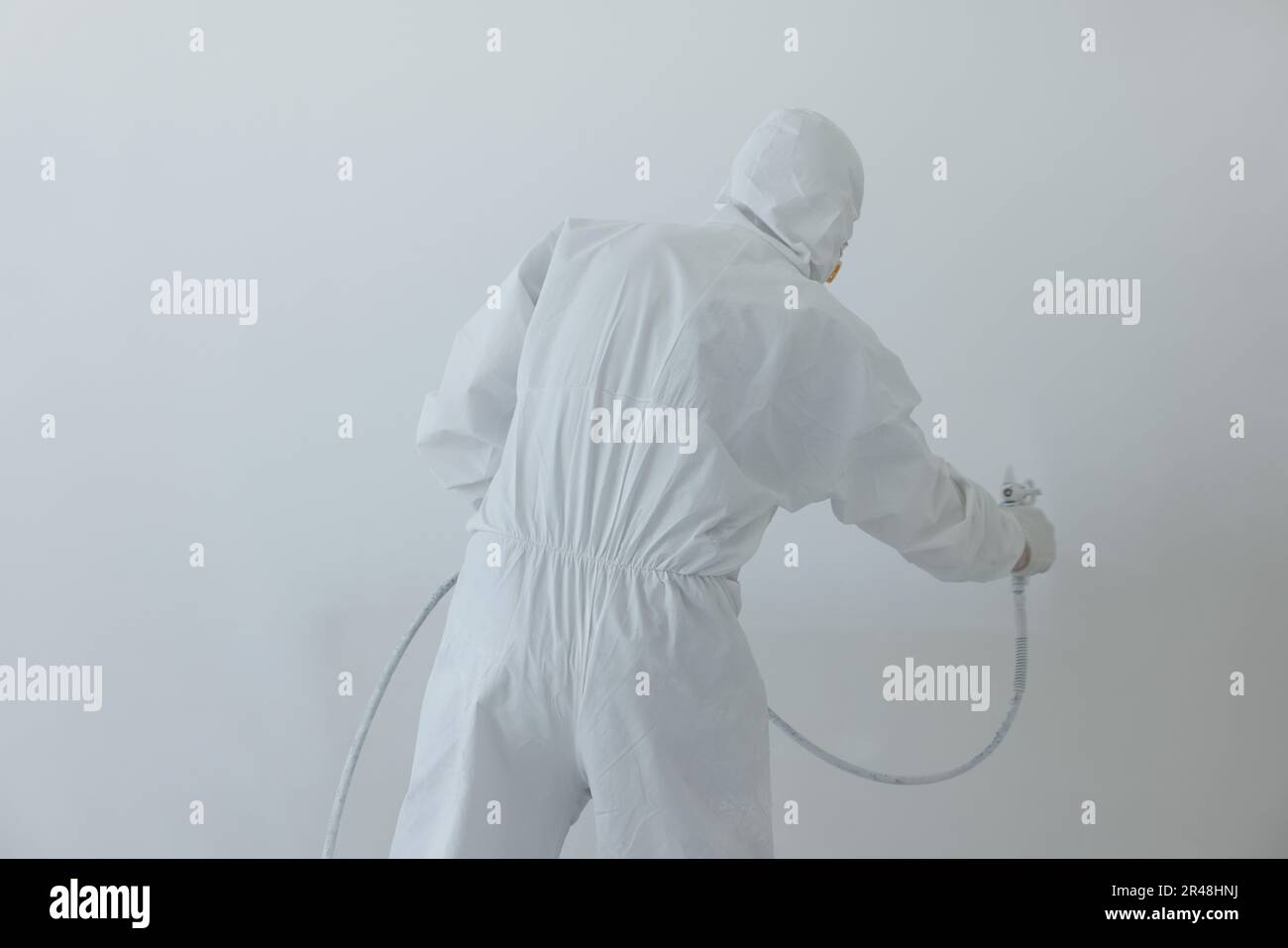 Decorator painting wall with spray, back view Stock Photo - Alamy