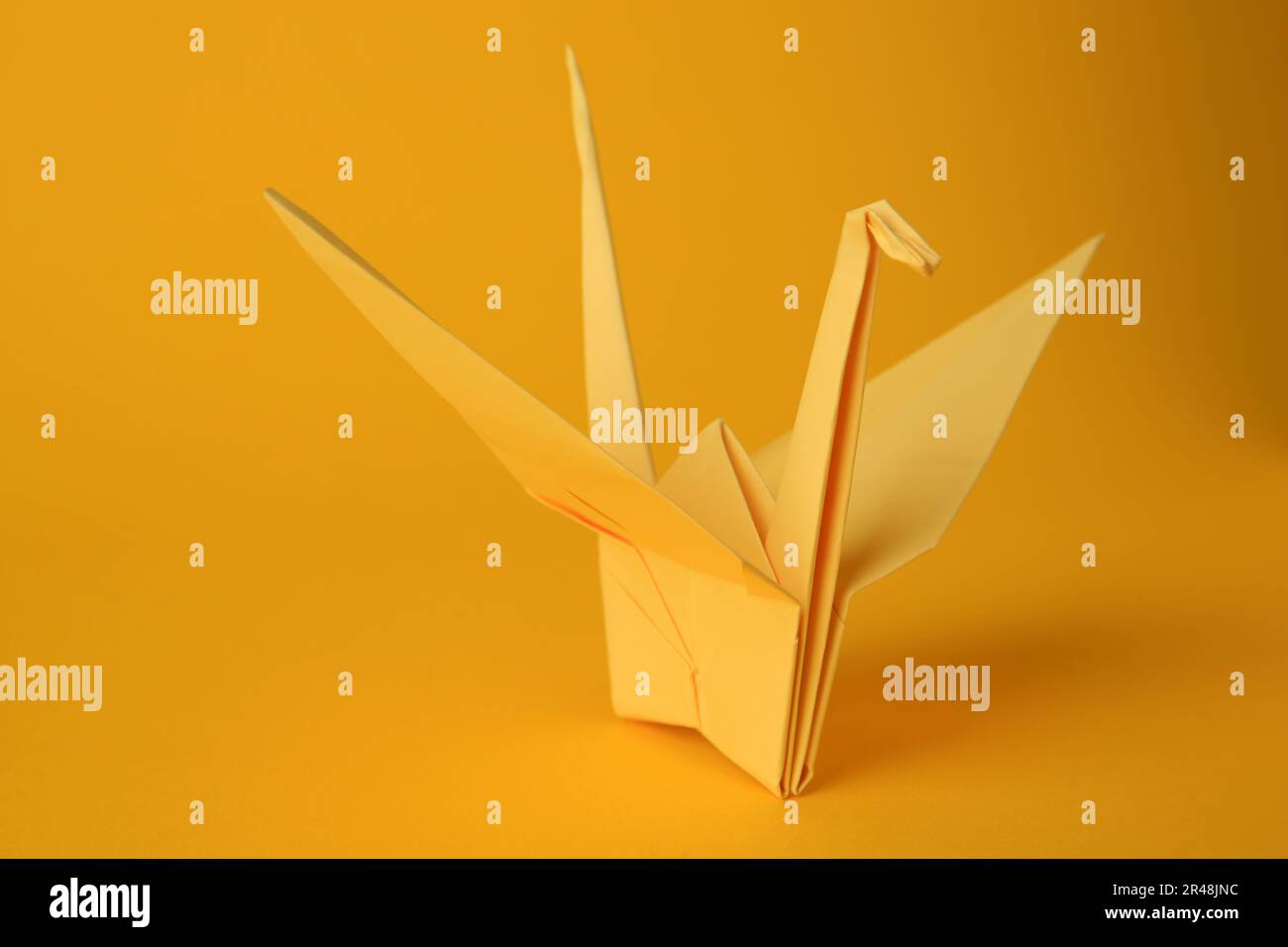 Origami art. Beautiful light yellow paper crane on orange background ...