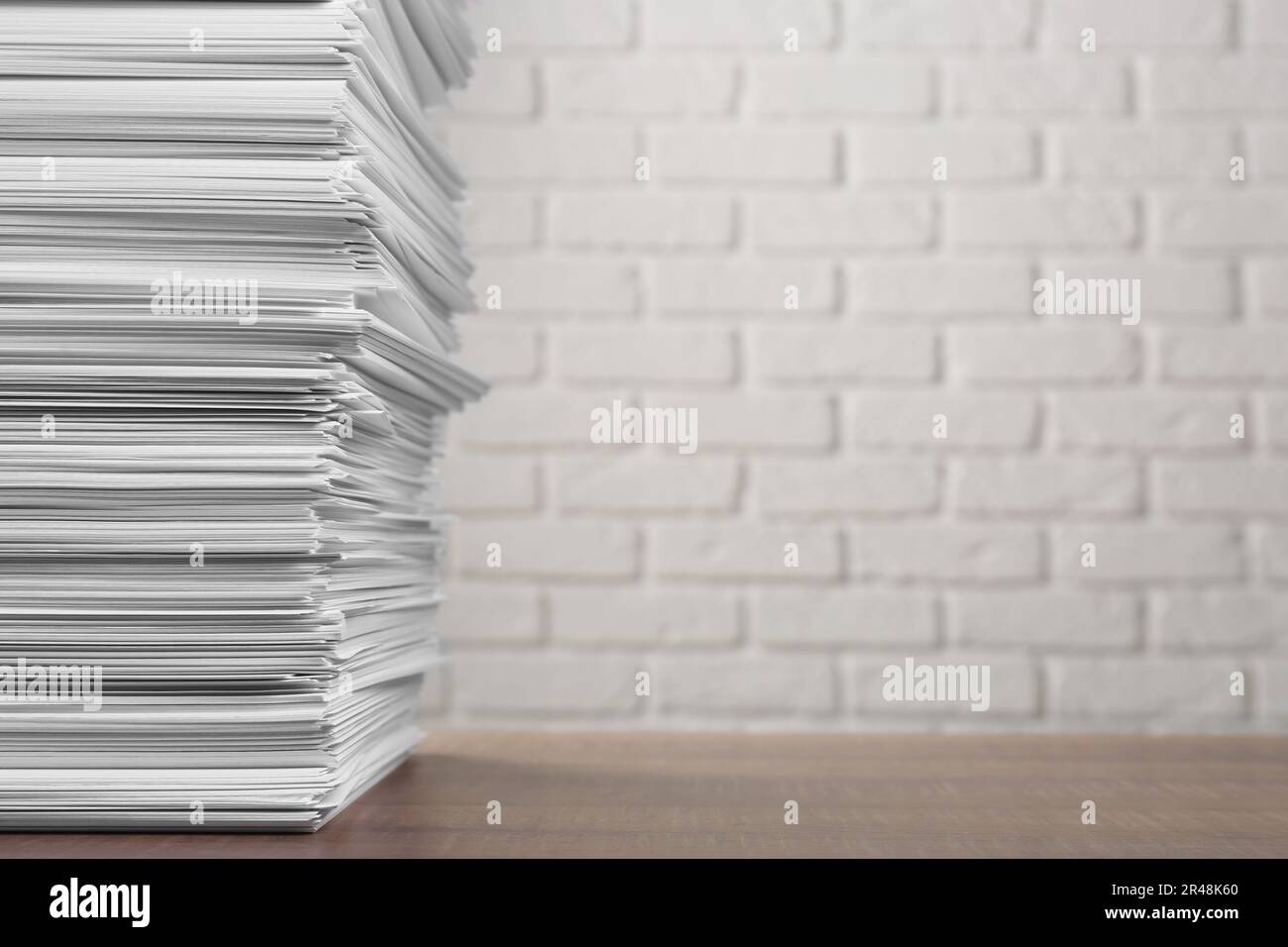 Stack of paper sheets on wooden table near white brick wall, space for ...
