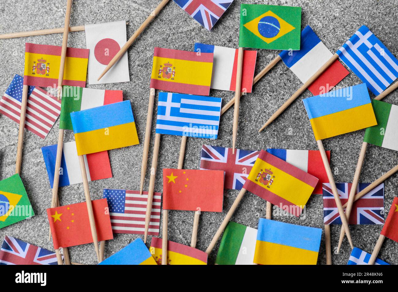 Many small paper flags of different countries on grey table, flat lay ...